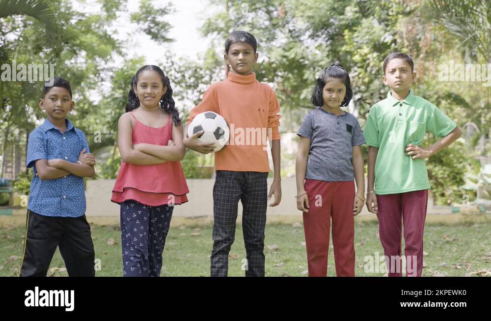 team of kids with football standing confidently by looking camera at ...