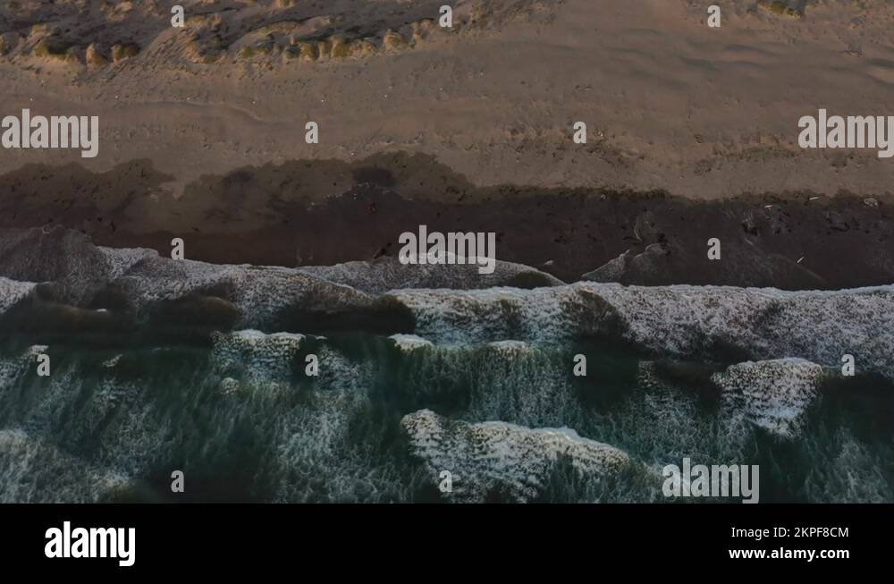 arial top down view of flat ocean waves crashing on a sand dune beach ...