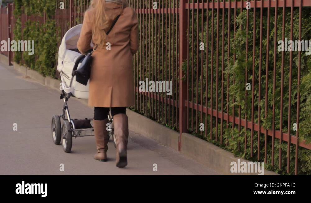 Rear view of mother with newborn child in buggy on street pathway ...