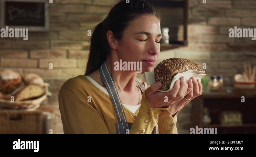 Close up of female artisan baker smells fresh baked bread taken out of ...