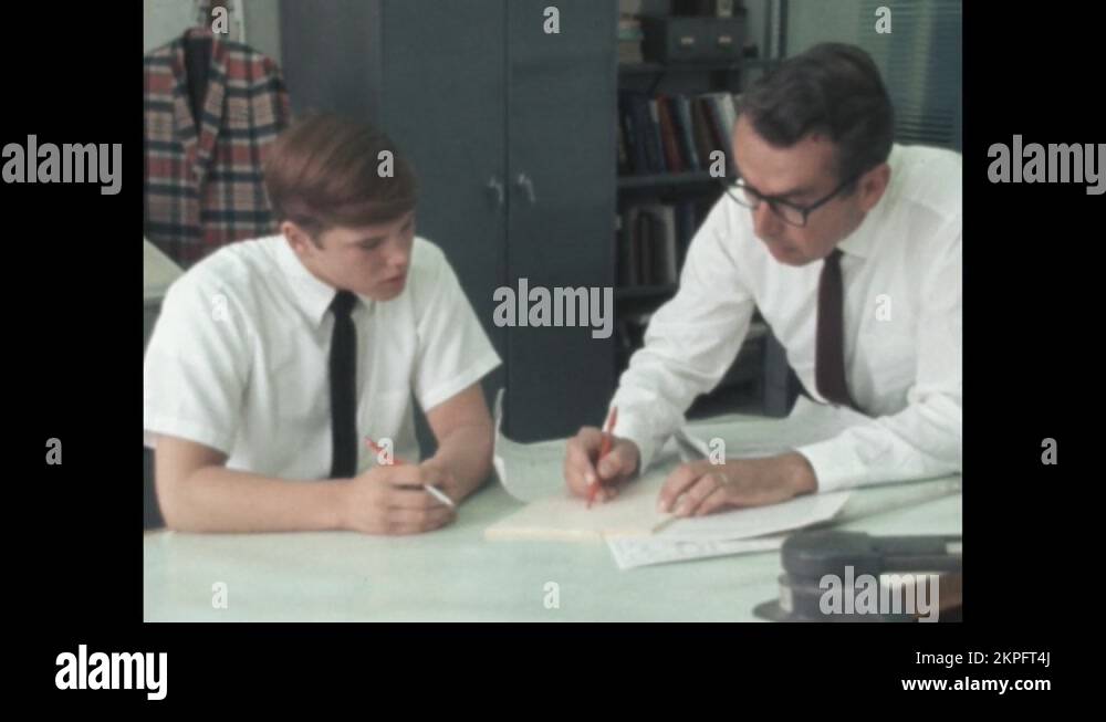 1960s: Two men sit at drafting table. Man draws on paper, talks to ...