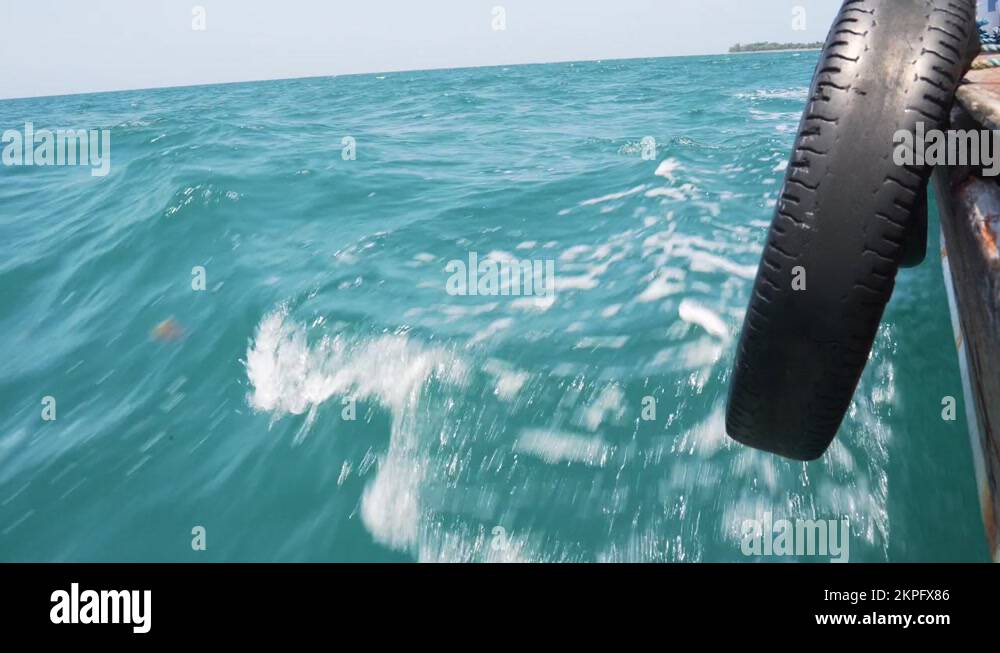 Tire tied to hull of boat cruising on azure sea waves, action shot ...