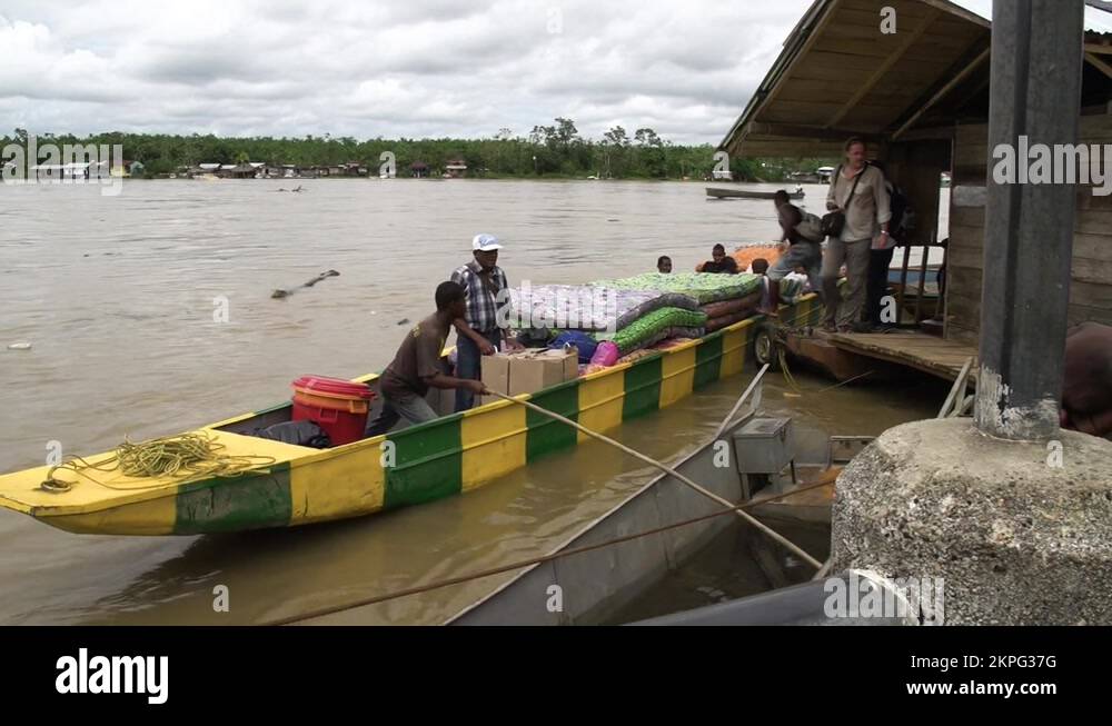 A green and yellow long river boat loading passengers on a massive ...