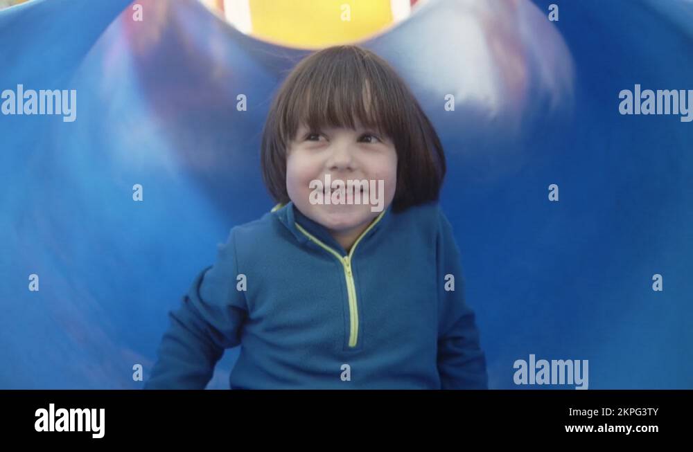 Little cute boy sliding off slide looking at camera posing in portrait ...