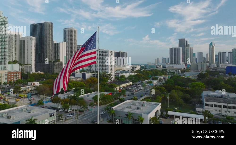Fly around American national flag waving on pole above city. High rise ...