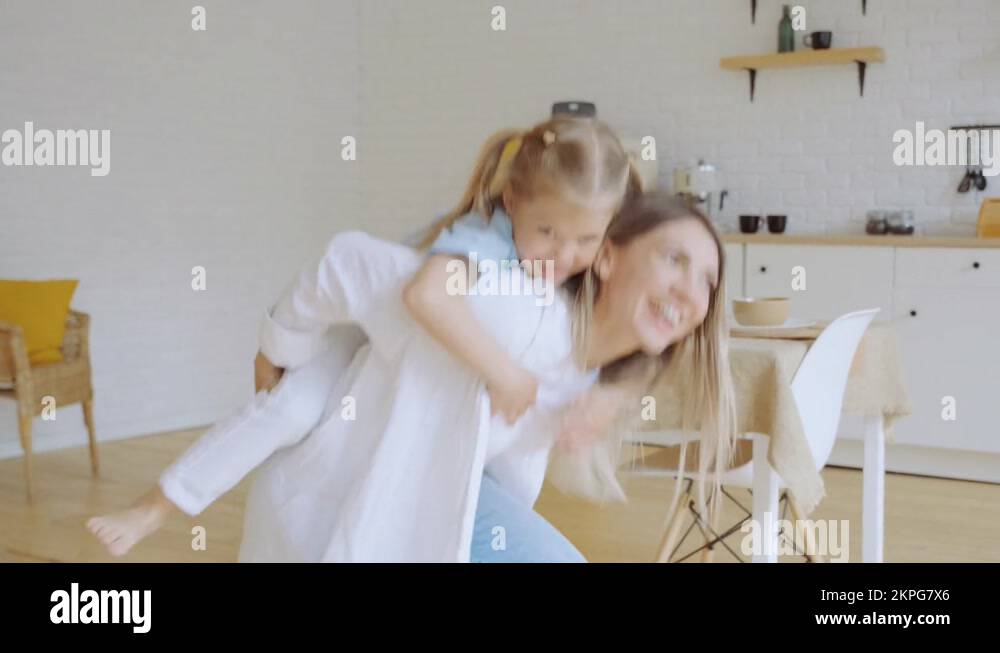 Little girl daughter run behind her mother and jumps on her back, she ...