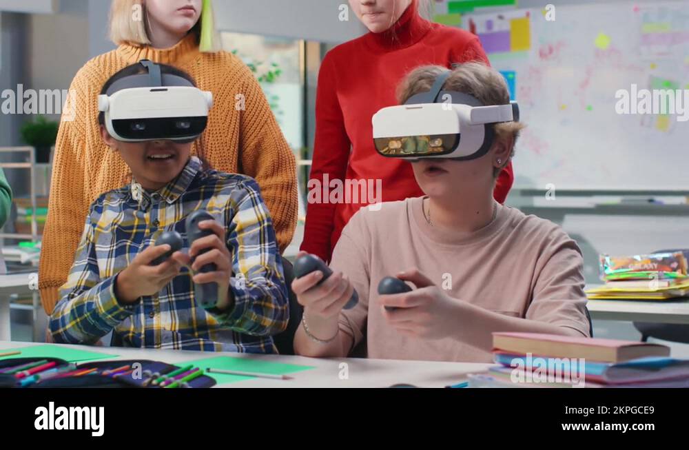 Teenagers looking at classmates in vr headset and joystick playing game ...