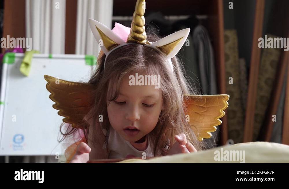 A cute little girl in a unicorn costume with wings is watching a ...
