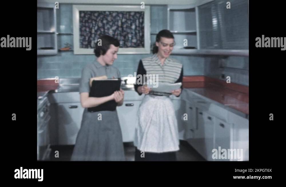 1950s: Two teen girls walk out of home ec classroom kitchen and look at ...