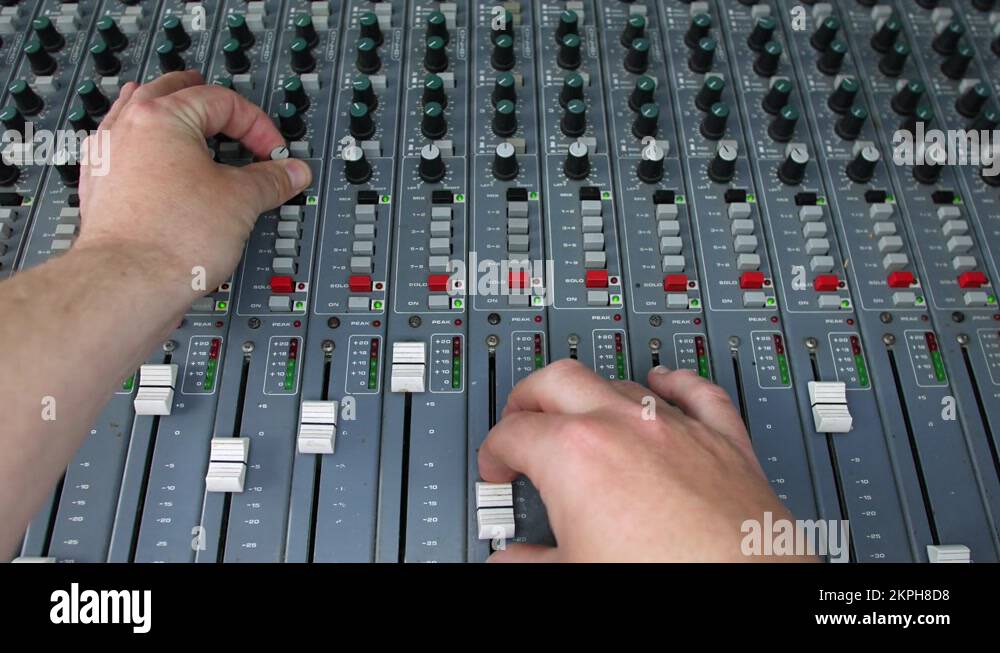An audio engineer mixing on a studio mixer console desk. The man is ...