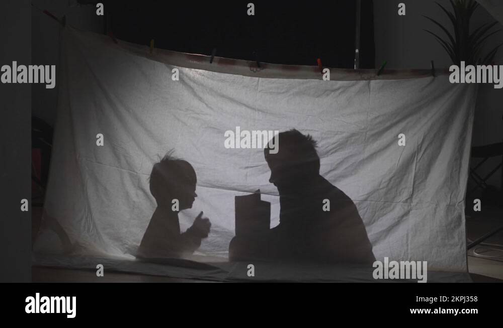 Boy telling a story to his little brother under a sheet tent lit by a ...