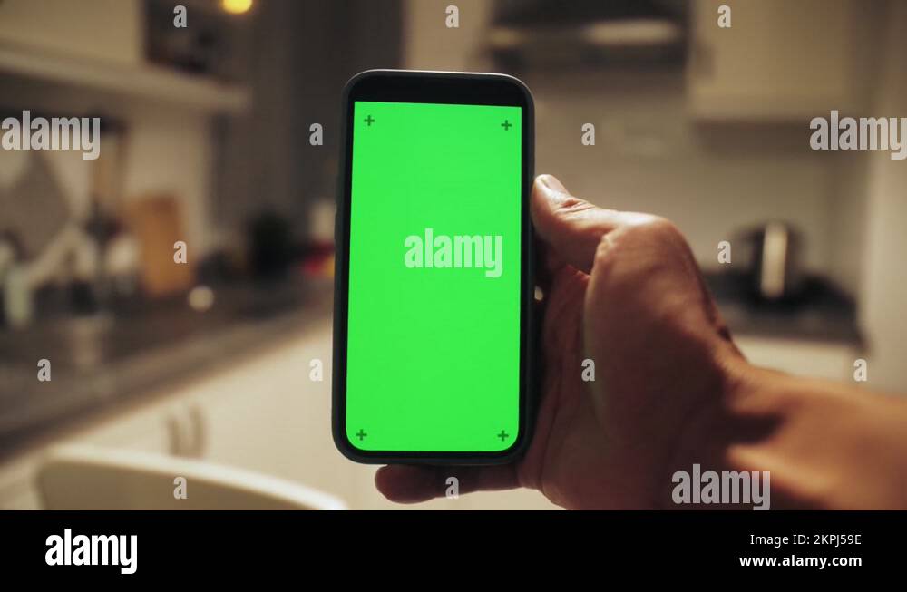 Man holding mobile phone with green screen at night in kitchen. Mock up ...