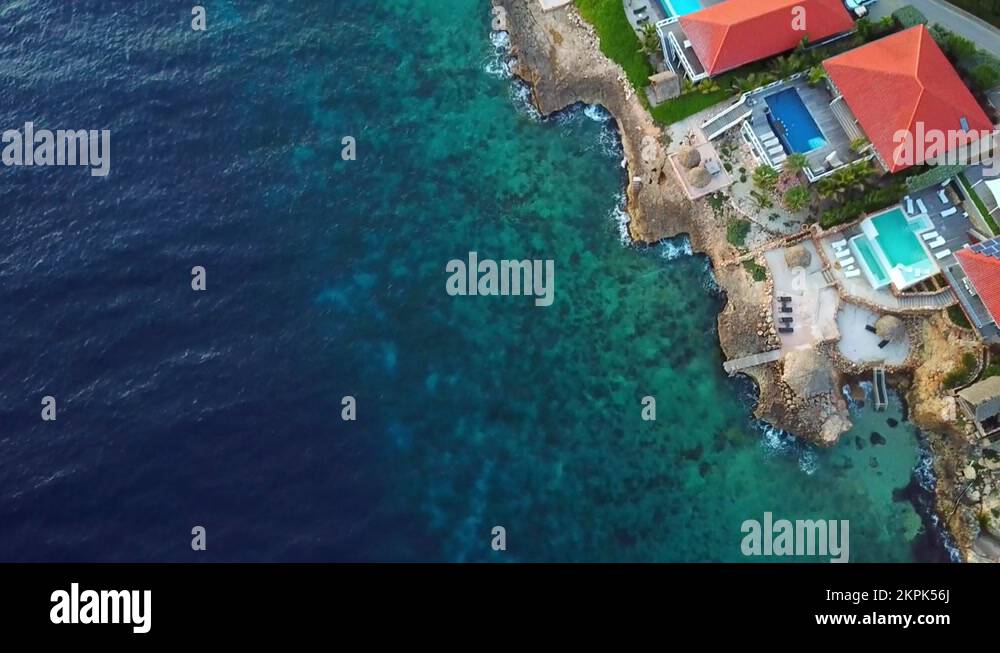 Overhead dolly-in aerial view of mansions on the shore of Jan Thiel ...