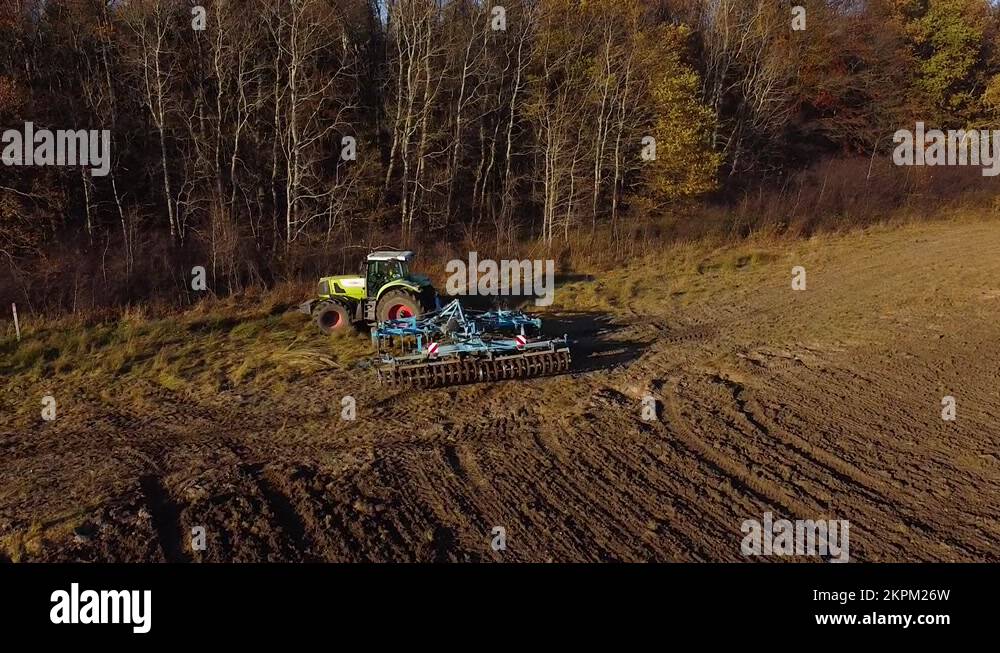 A tractor with a plow turns on the border of a field and a forest Stock ...