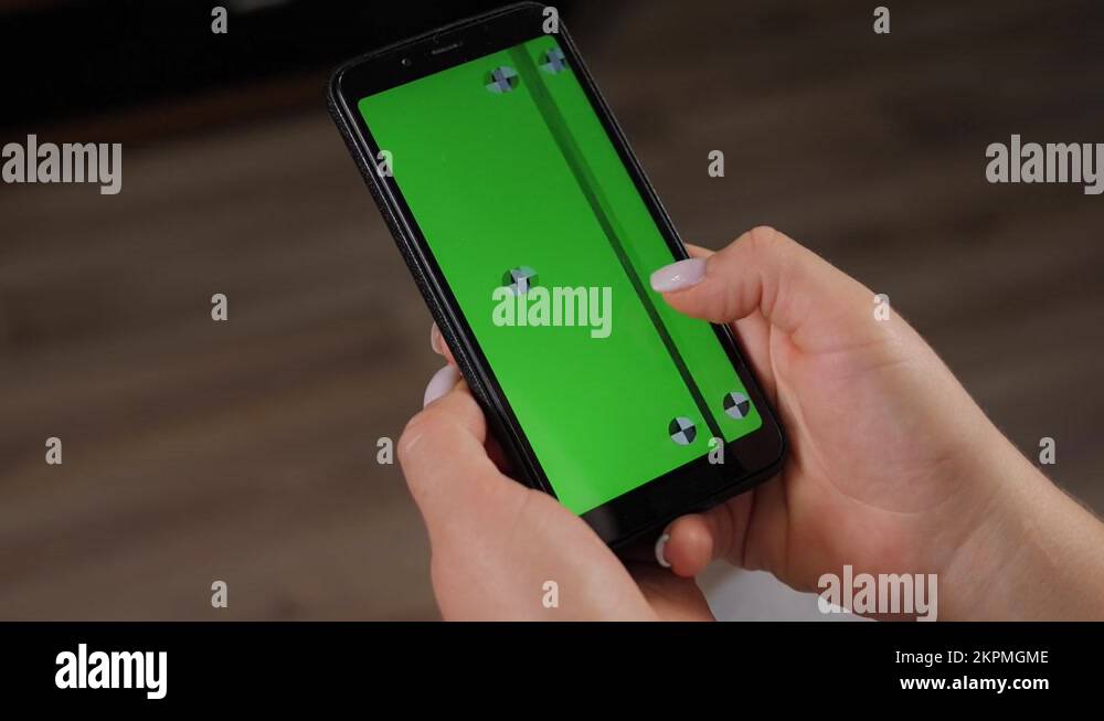 Close-up of woman's hand browsing smartphone with green screen at home ...