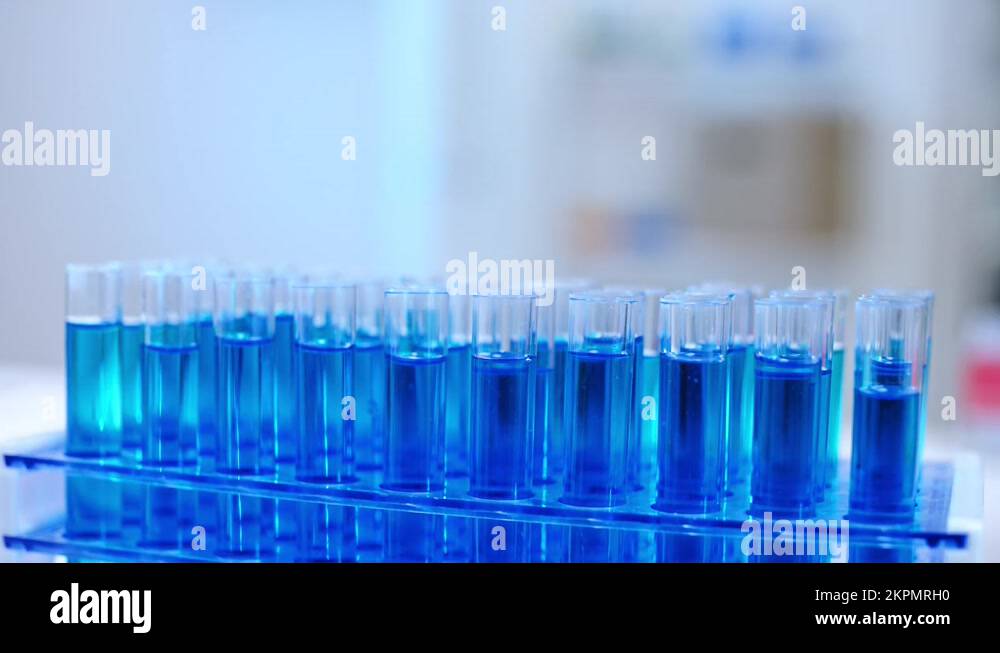 Close-up of pipette dripping chemical liquid into glass flasks with lab ...