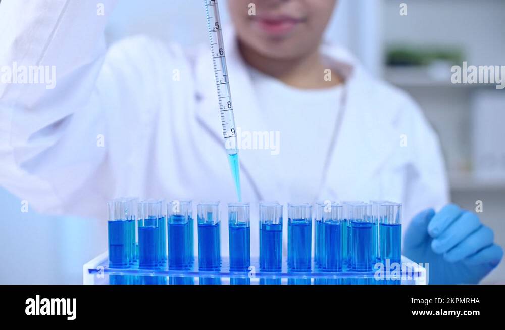 Lab assistant adding reagent to glass flasks with sample liquid ...