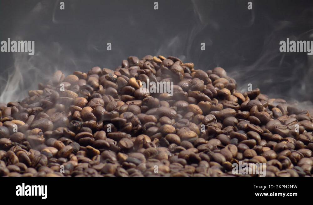 Steam rising coffee beans heap close up. View process roasting caffeine ...