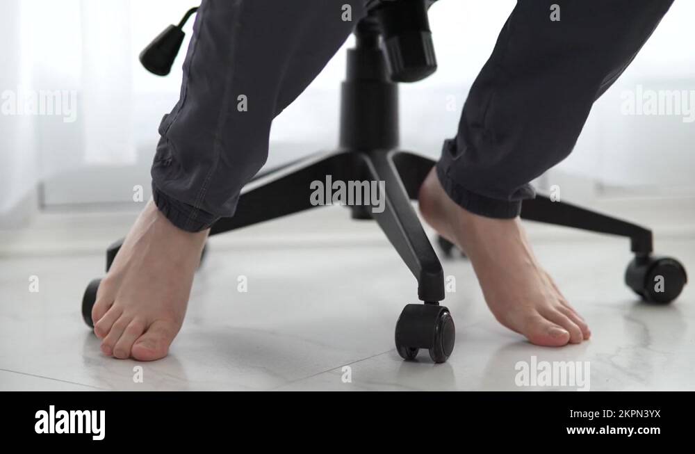 Barefoot men's feet on an office chair with wheels on white porcelain ...