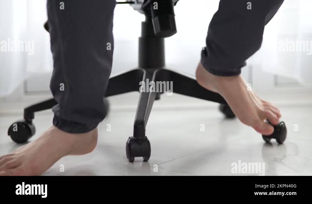 Barefoot men's feet on an office chair with wheels on white porcelain ...