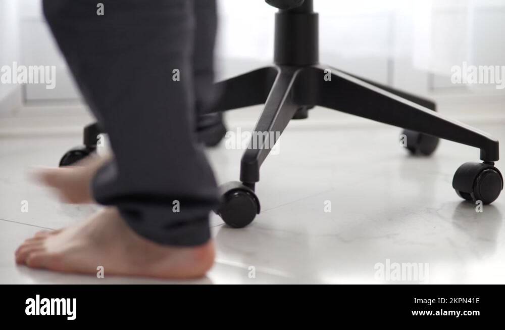 Barefoot men's feet on an office chair with wheels on white porcelain ...