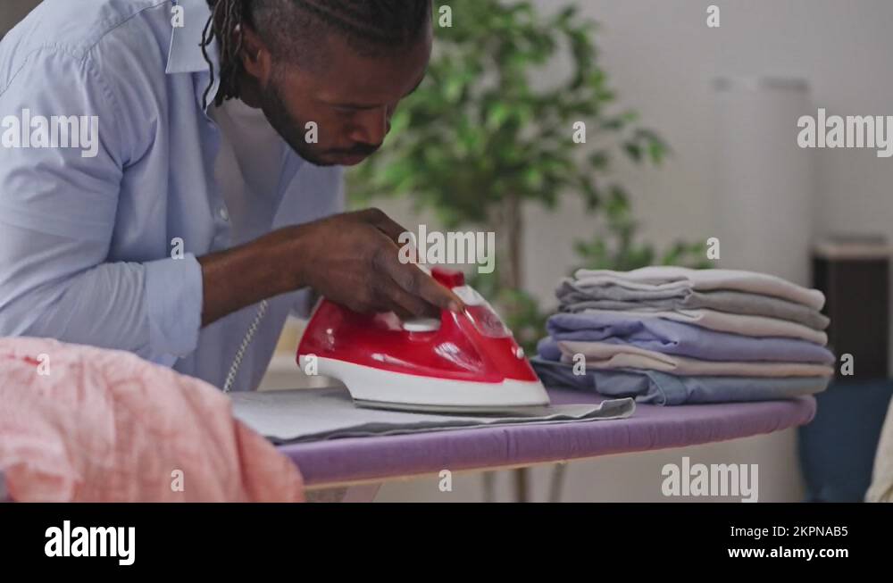 Concentrated African American man meticulously ironing clothes, daily ...