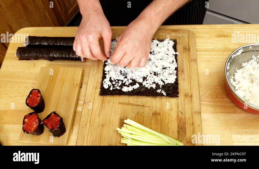Spreading cooked rice onto edible sheet of sea weed and placing pieces ...