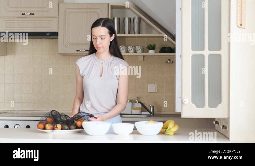 Woman puts ripe fruit in a plate in the kitchen. Vegetarianism, healthy ...