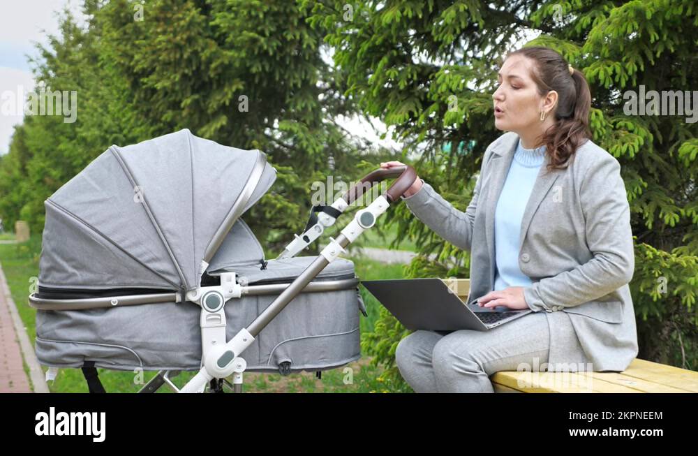 Mother freelancer works on laptop calming baby in stroller Stock Video ...