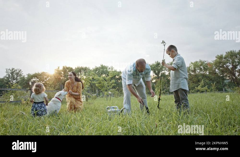 Family planting tree and caressing dog. Ground level of father and son ...