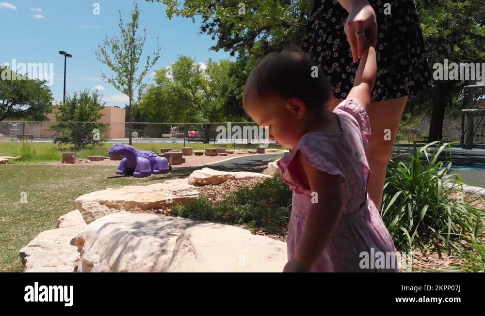 Toddler walking down stone steps at a playground with mom. Park is ...