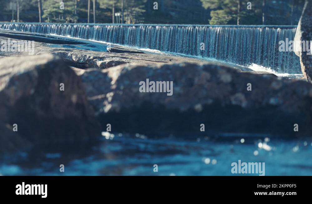 Water cascading from the concrete ramp in the shallow river. Sun flares ...
