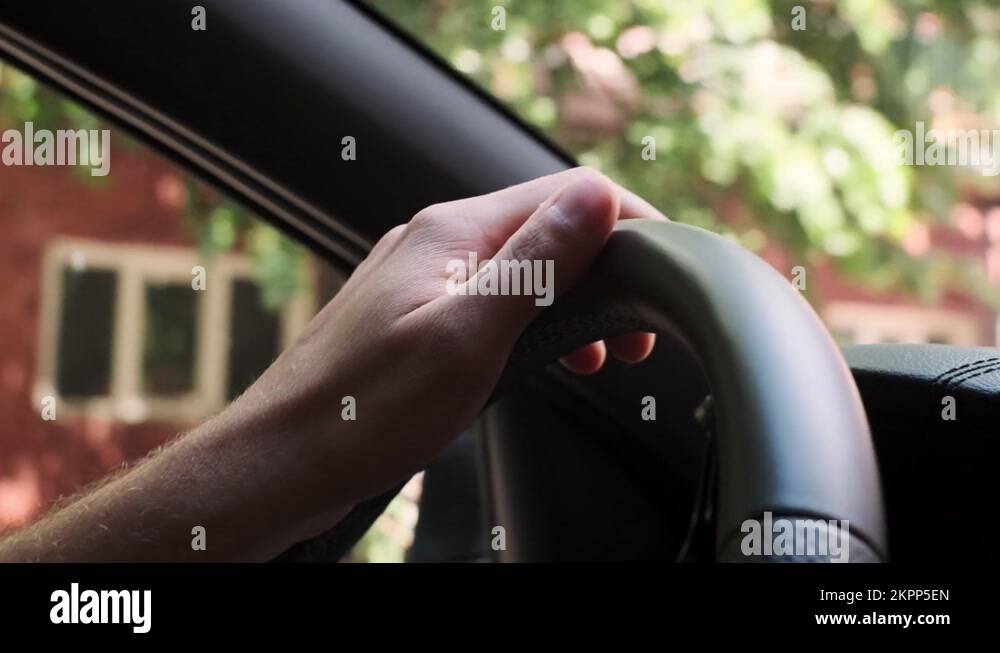 Handheld close up view of man hand turning steering wheel in car ...
