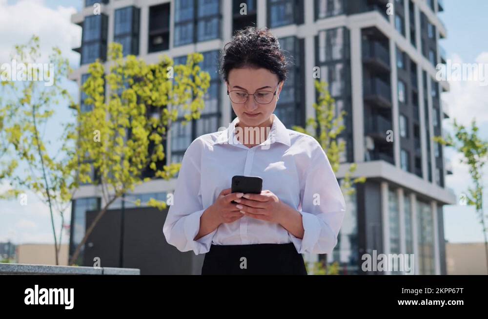 Lady tapping messaging on mobile phone app near office on the street ...