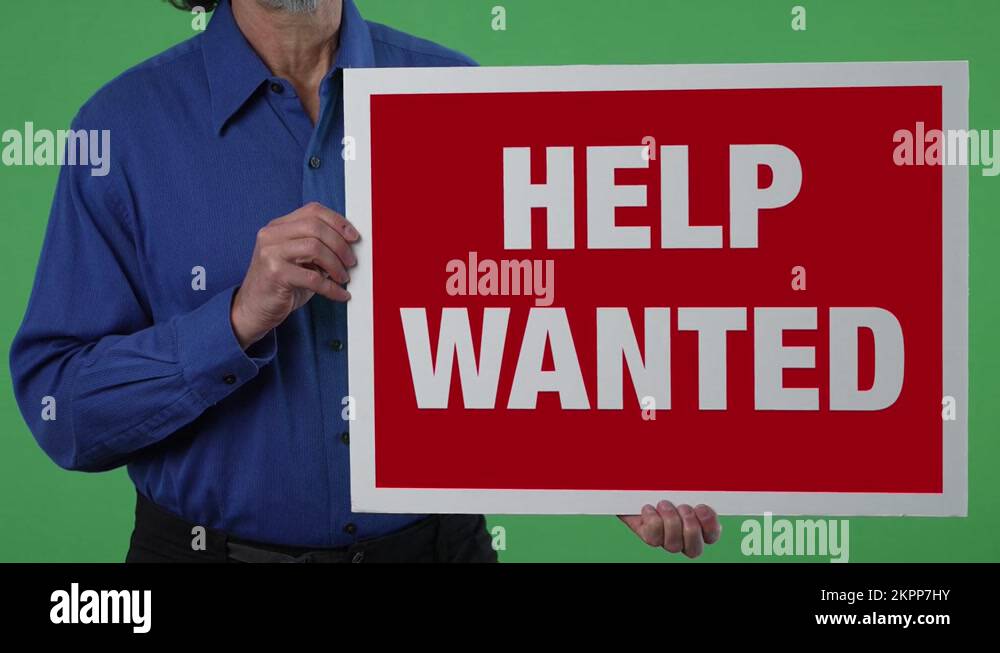Man in white shirt holds Help Wanted sign on solid green screen chroma ...
