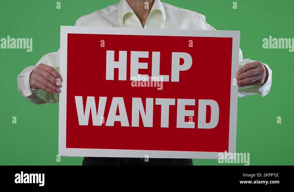 Man in blue shirt holds Help Wanted sign on solid green screen chroma ...