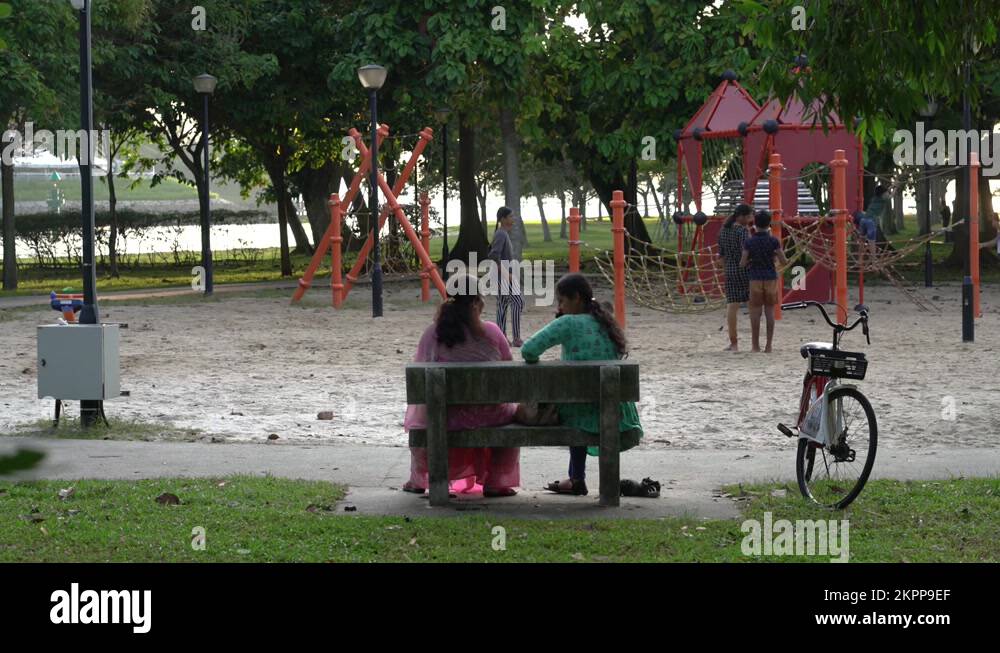 Two Indian ladies talk at the park overlooking kids playground , Changi ...