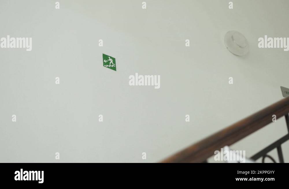 Green sign indicating the exit direction on white wall near a staircase ...