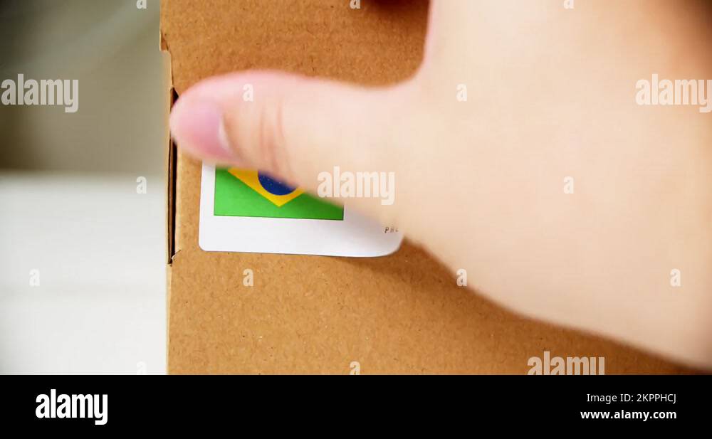 Hands applying MADE IN BRAZIL flag label on a shipping cardboard box ...