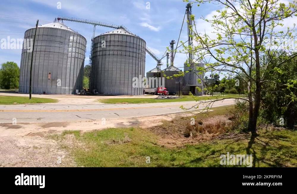 Pan reveal Red semi truck parked at a grain silo filling up in rural ...
