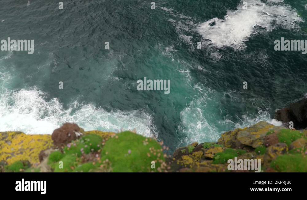 Waves gently crash over rocks and against the base of a sea cliff in ...