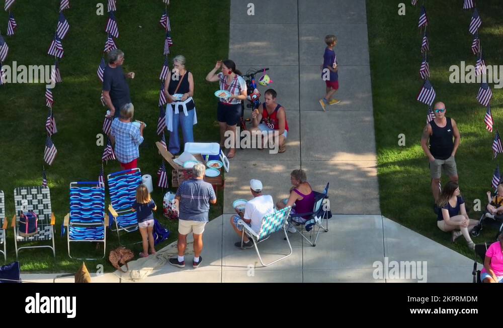 Family and friends gather on sidewalk for picnic. USA flags in yard ...