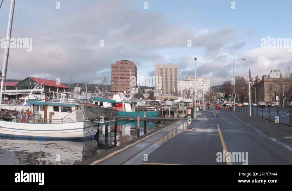 Pedestrians walk down footpath along Davey Street in Hobart with boats ...