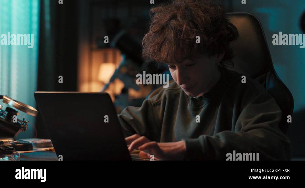 Teenage boy doing homework using computer sitting by desk in room alone ...