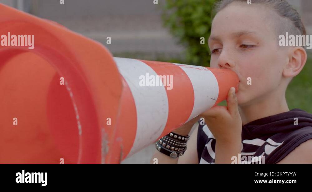 The child speaks into traffic cone. He holds it with his hands, puts it ...