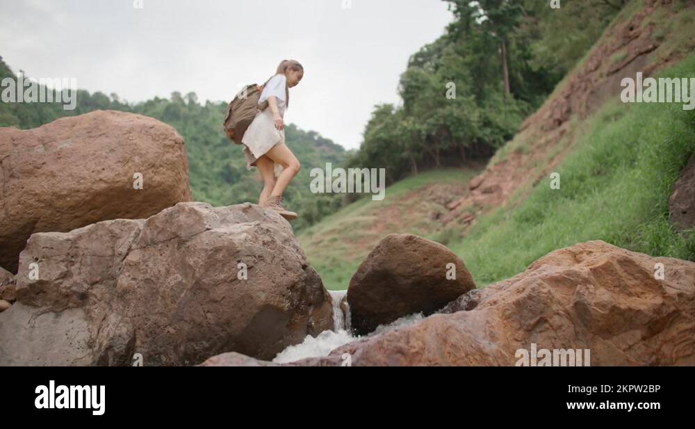 Young woman traveller jumping on the rock over stream on a forest trail ...