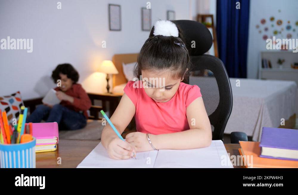 A little girl completing her school assignment sitting at her desk ...
