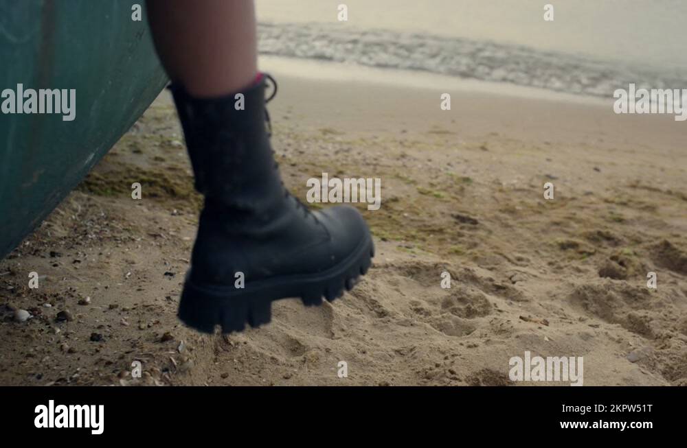 Woman leg wearing black boot hanging from old boat standing sand beach ...