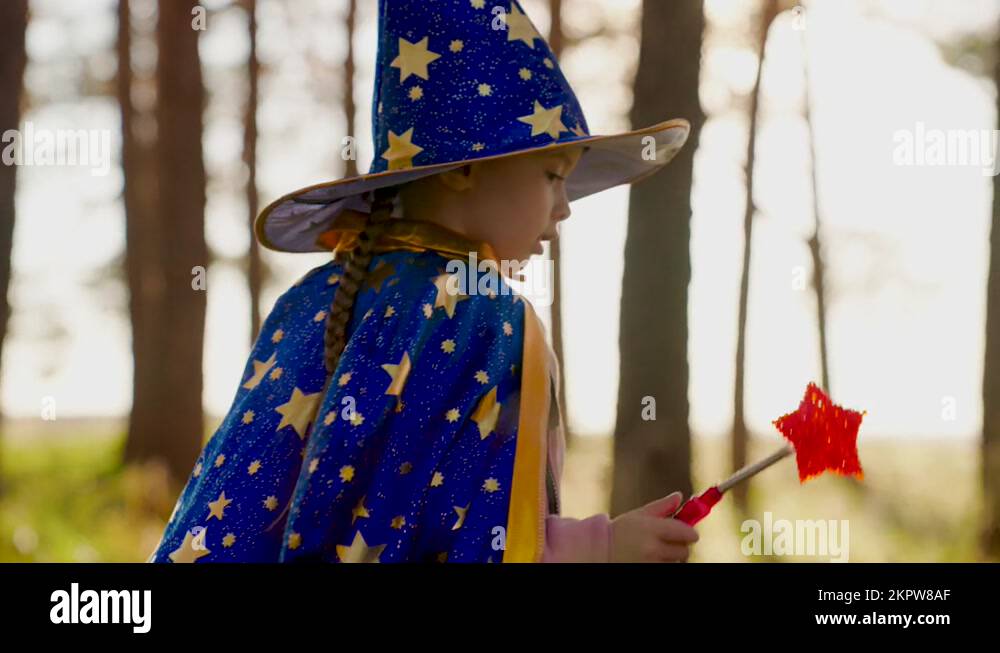 Girl, child plays in wizard costume, raises her hands, waves magic wand ...