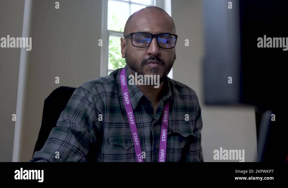 A close up shot from behind an office desk of an Indian man wearing ...